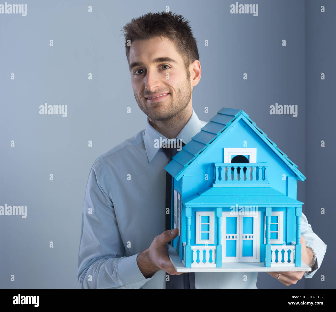 Friendly real estate agent with light blue model house Stock Photo - Alamy