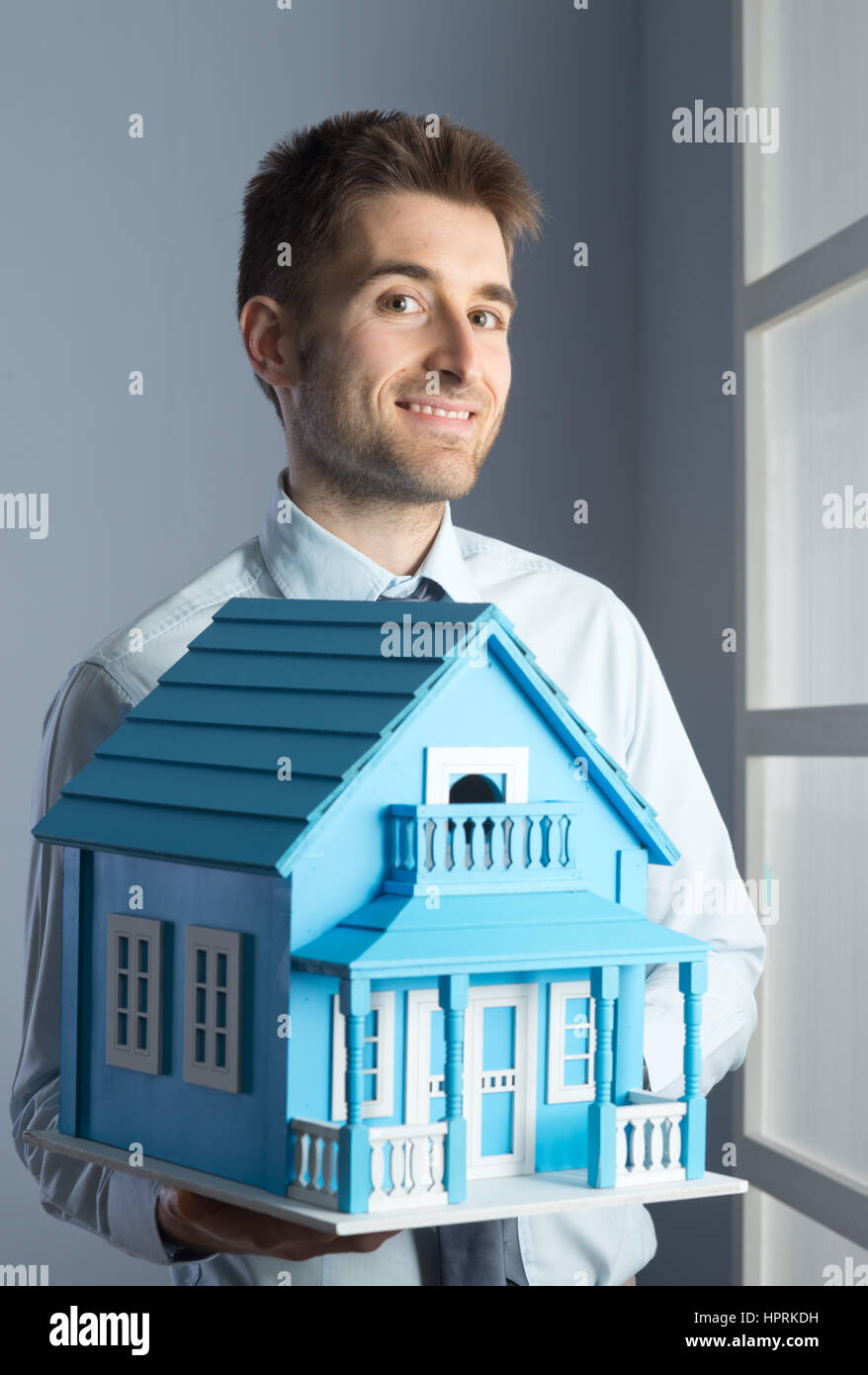 Friendly real estate agent with light blue model house Stock Photo - Alamy
