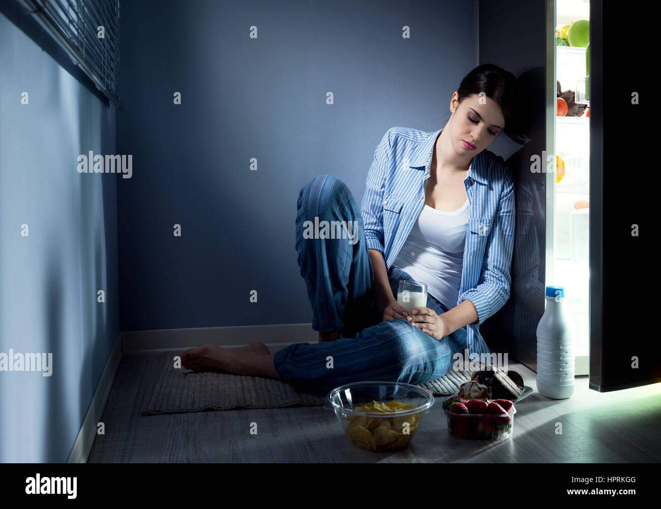 Sleepless sad woman sitting on kitchen floor having a glass of milk ...
