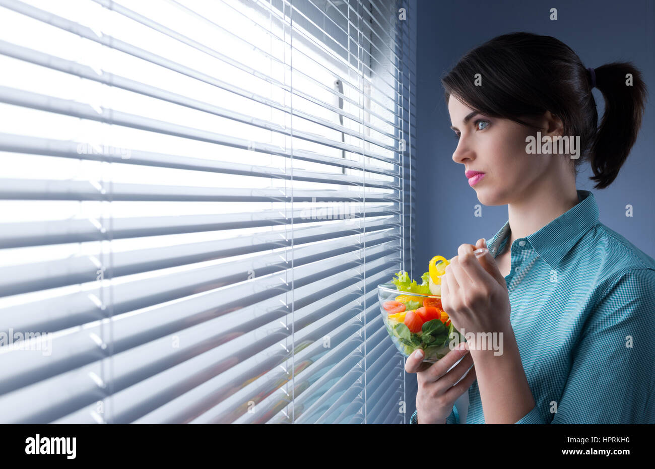 Pensive woman eating healthy salad in front of a window Stock Photo - Alamy