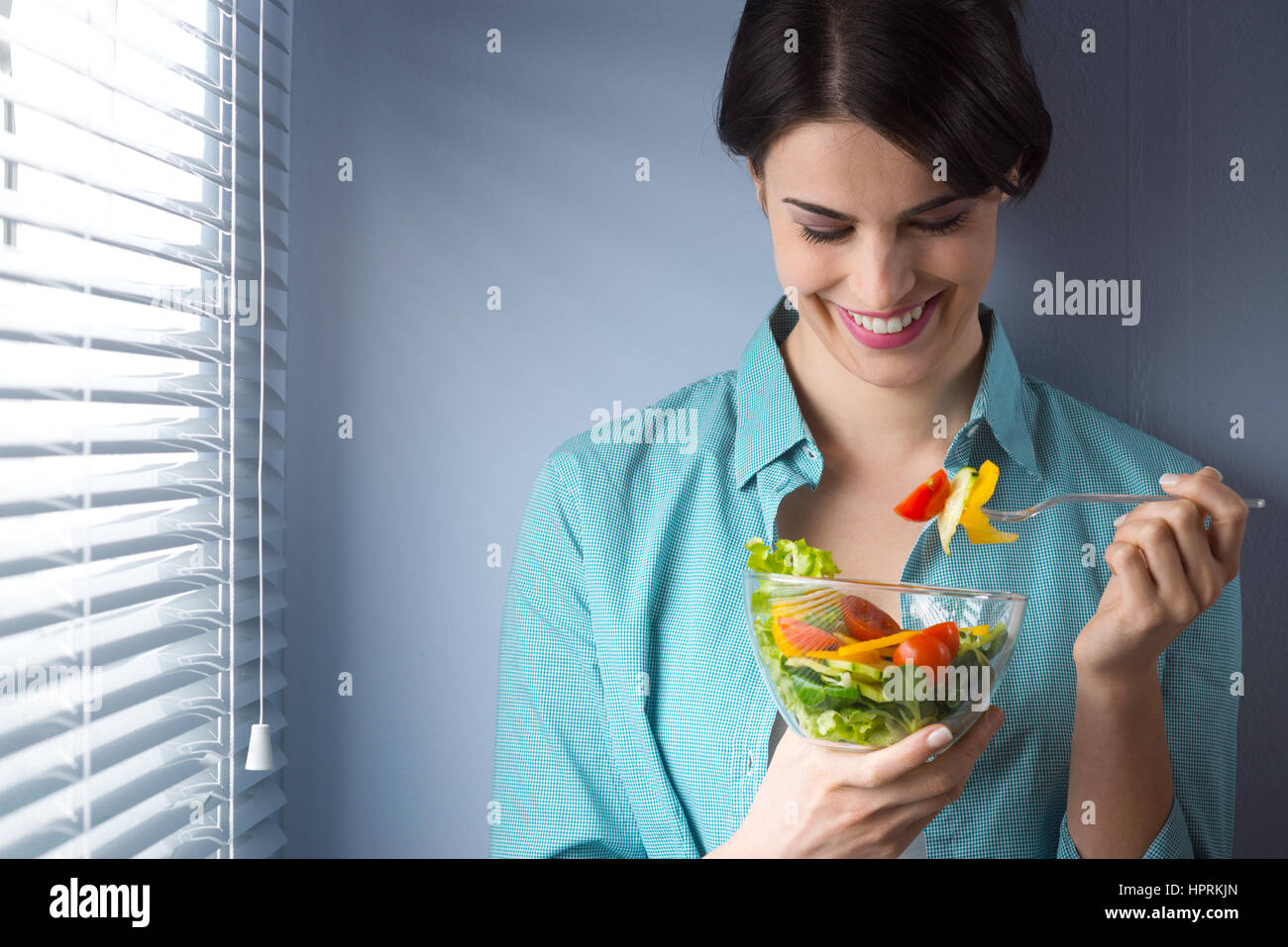 Woman smiling and eating salad in front of a window Stock Photo - Alamy