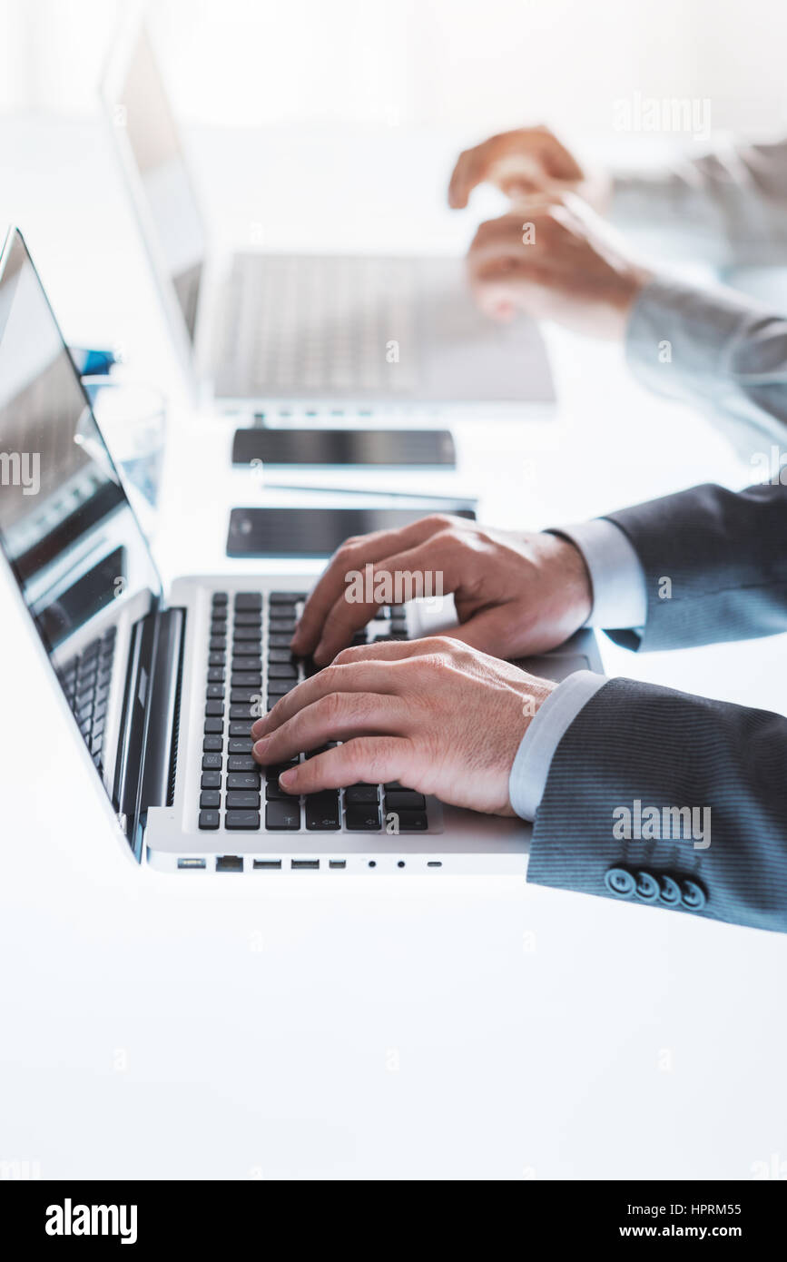 Professional businessmen working on laptops at office desk, hands close ...