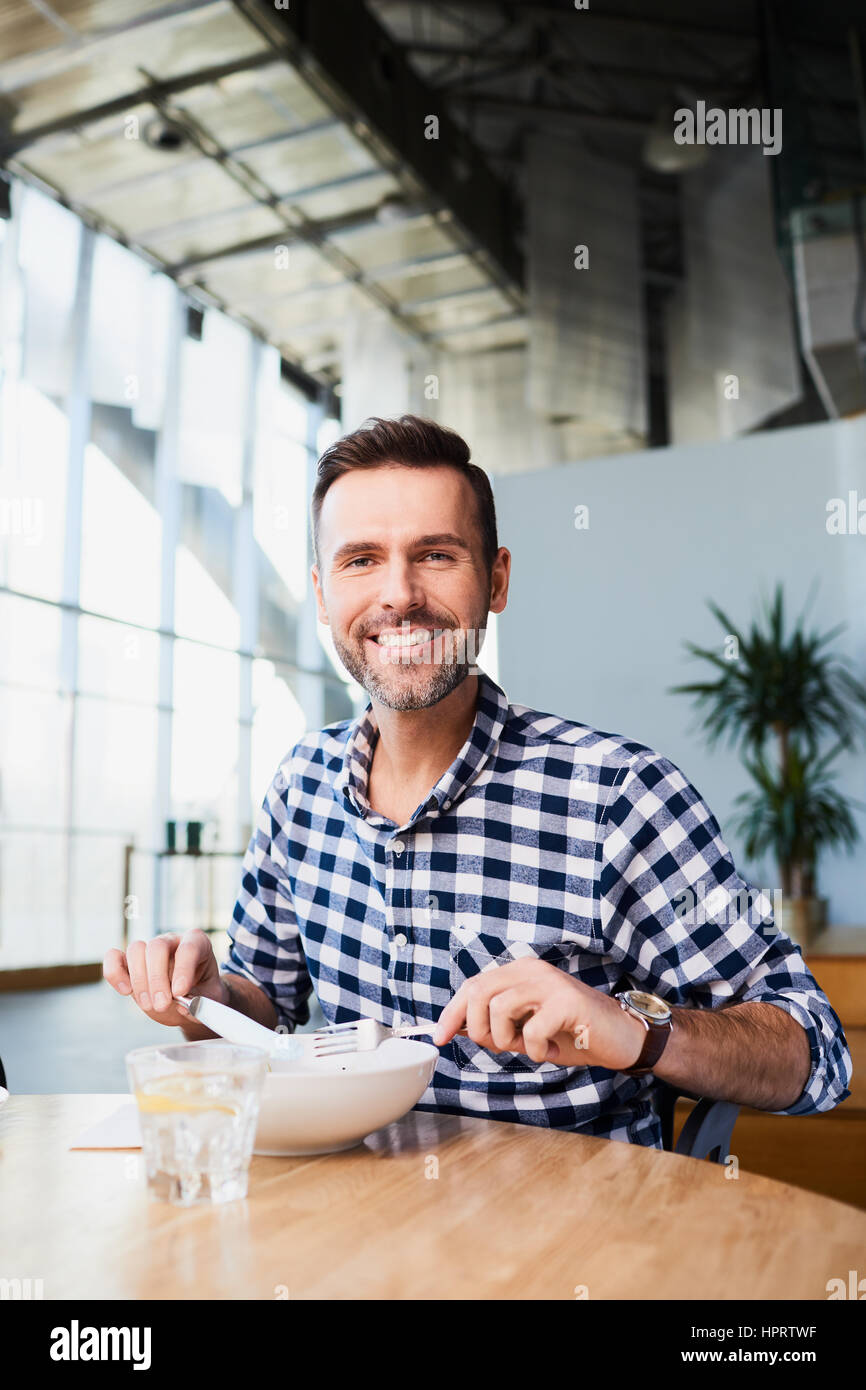 Handsome man in cafe eating with fork and knife in hands smiling and ...
