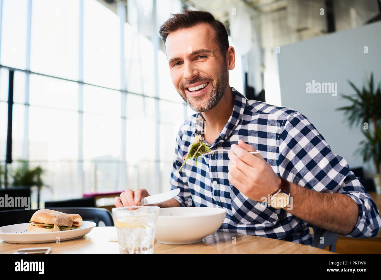 Handsome bearded man in checked shirt holding fork eating in cafe and ...