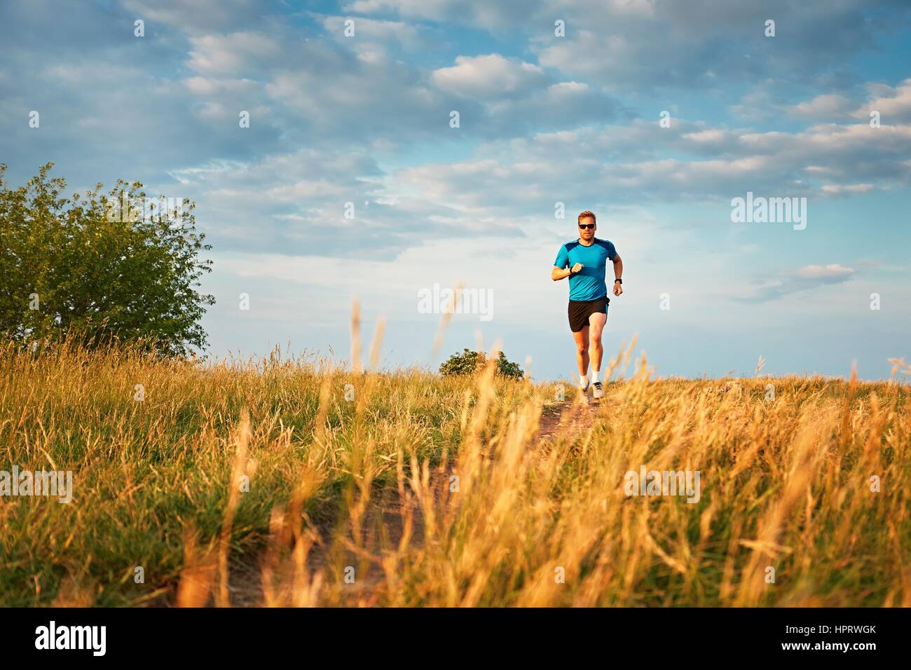 Sport lifestyle. Athletic young man is running on the hillside outside ...