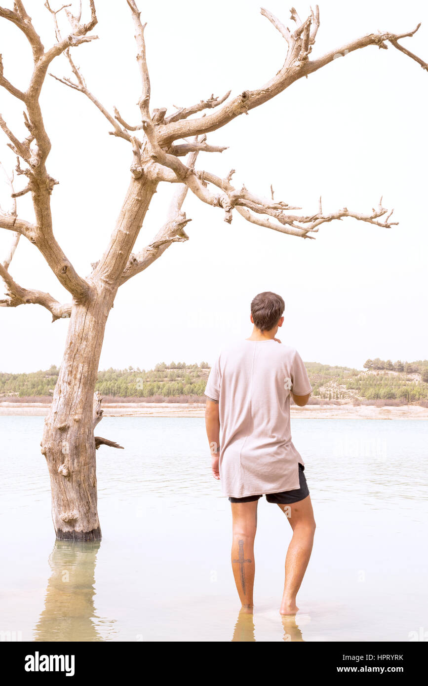 Young man looking out at a dead tree flooded by water. concept of ...