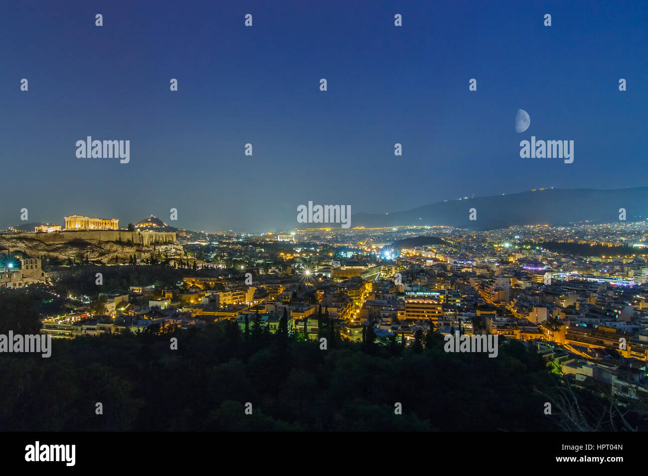 The Parthenon in Acropolis Hill in Athens, Greece shot in blue hour with the moon rising above ...