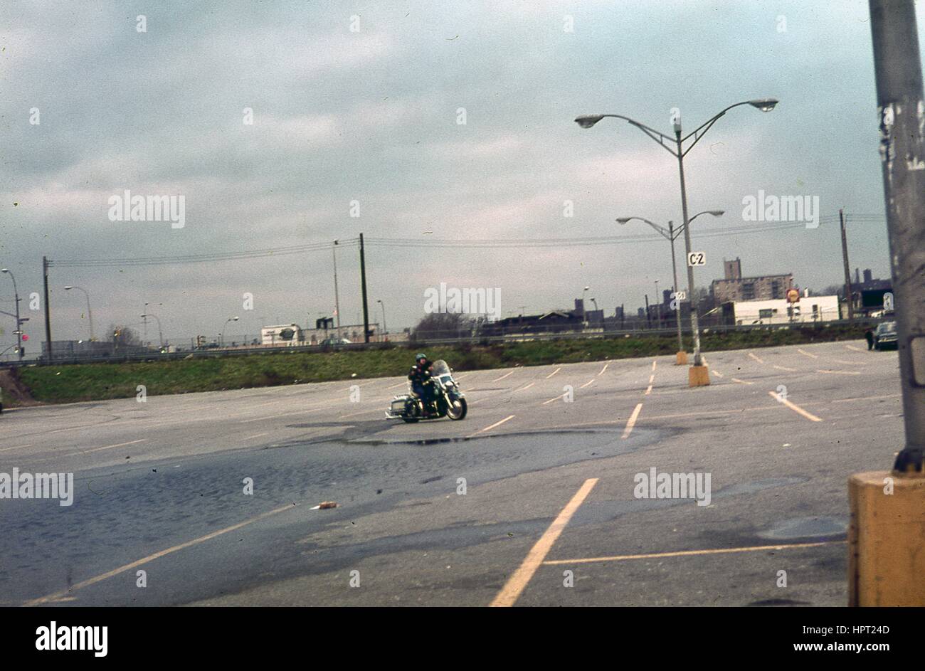 Two people ride on a motorcycle through an empty parking lot in the ...