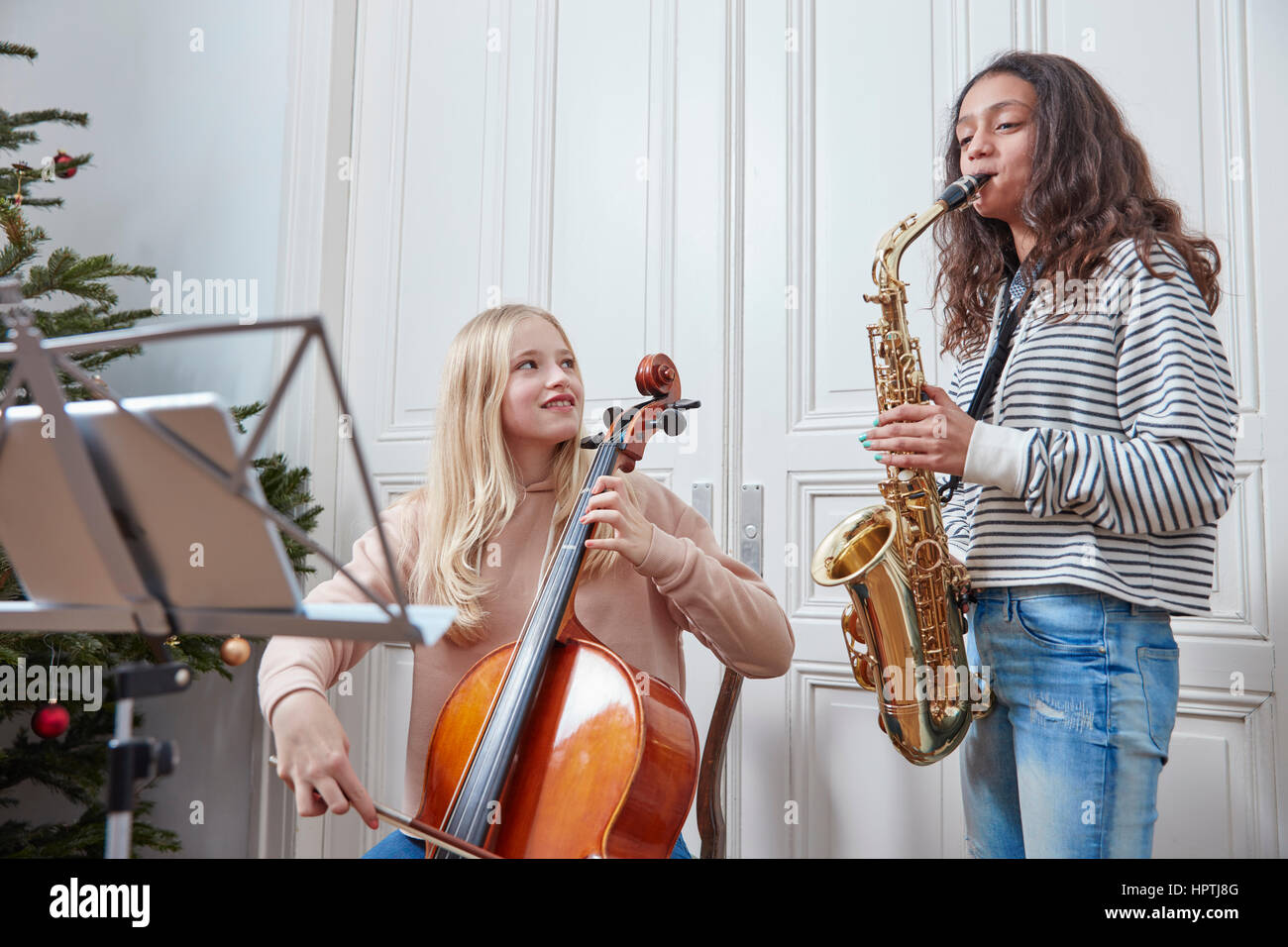 Two girls playing cello and saxophone at Christmas tree Stock Photo - Alamy