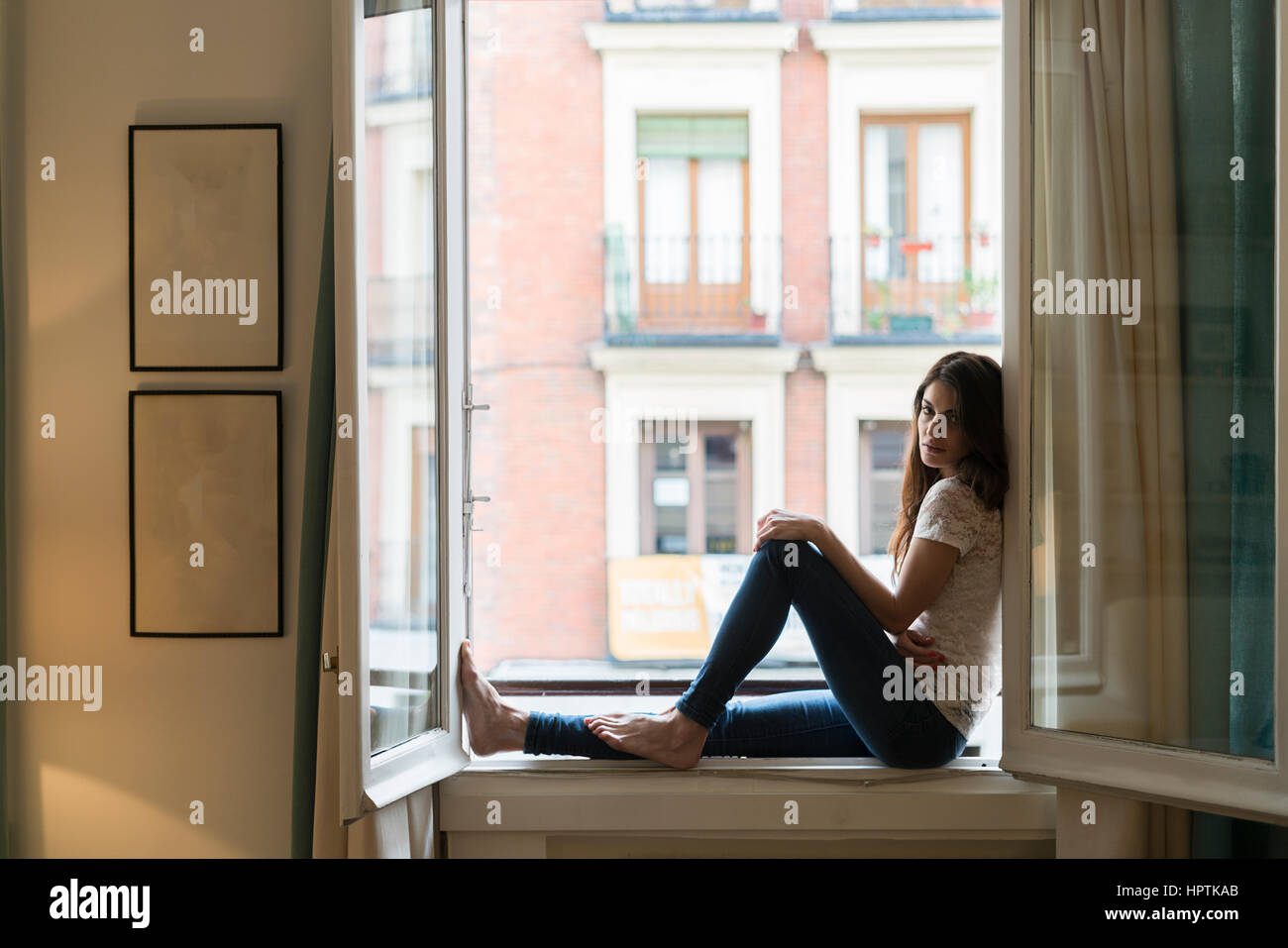 Woman sitting on window sill at open window Stock Photo - Alamy