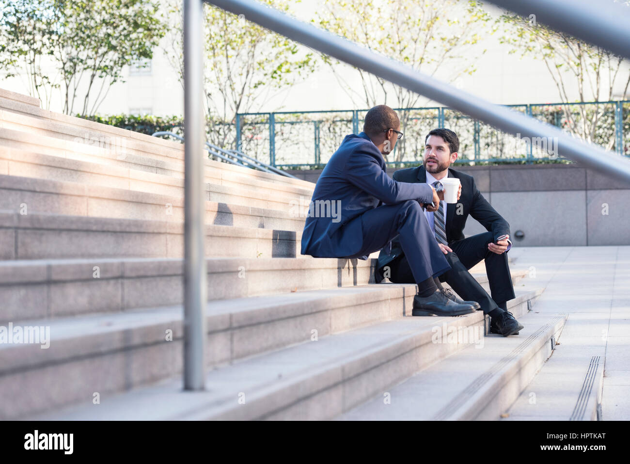 Two businessmen sitting on stairs talking Stock Photo - Alamy