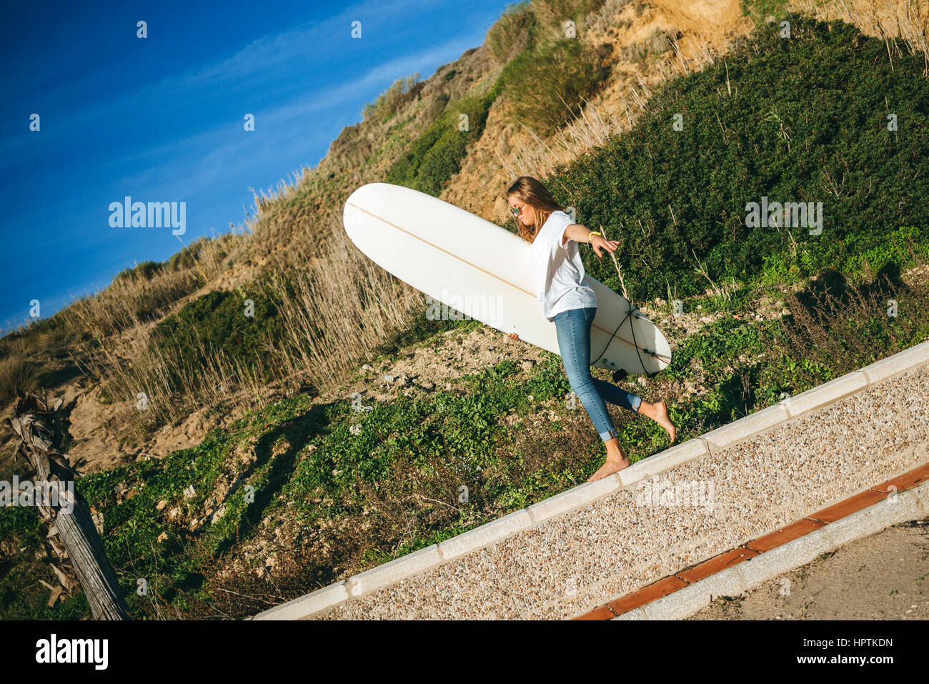 Young woman with surfboard balancing on wall Stock Photo - Alamy