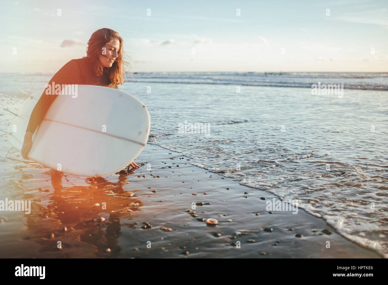 Young woman with surfboard crouching at seashore Stock Photo - Alamy