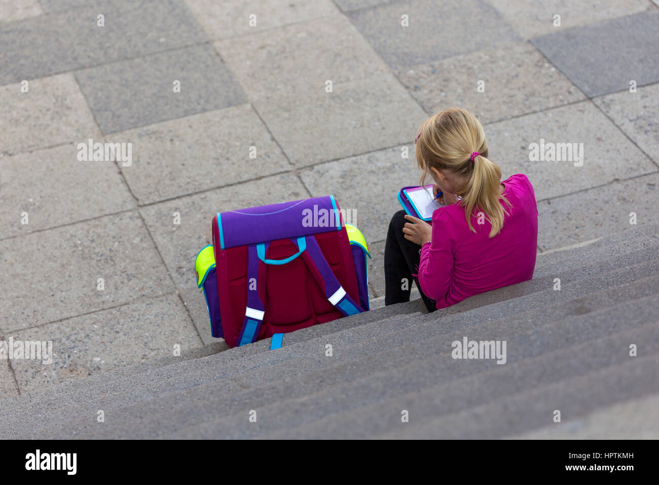 Back view of little girl with school bag sitting on stairs doing ...