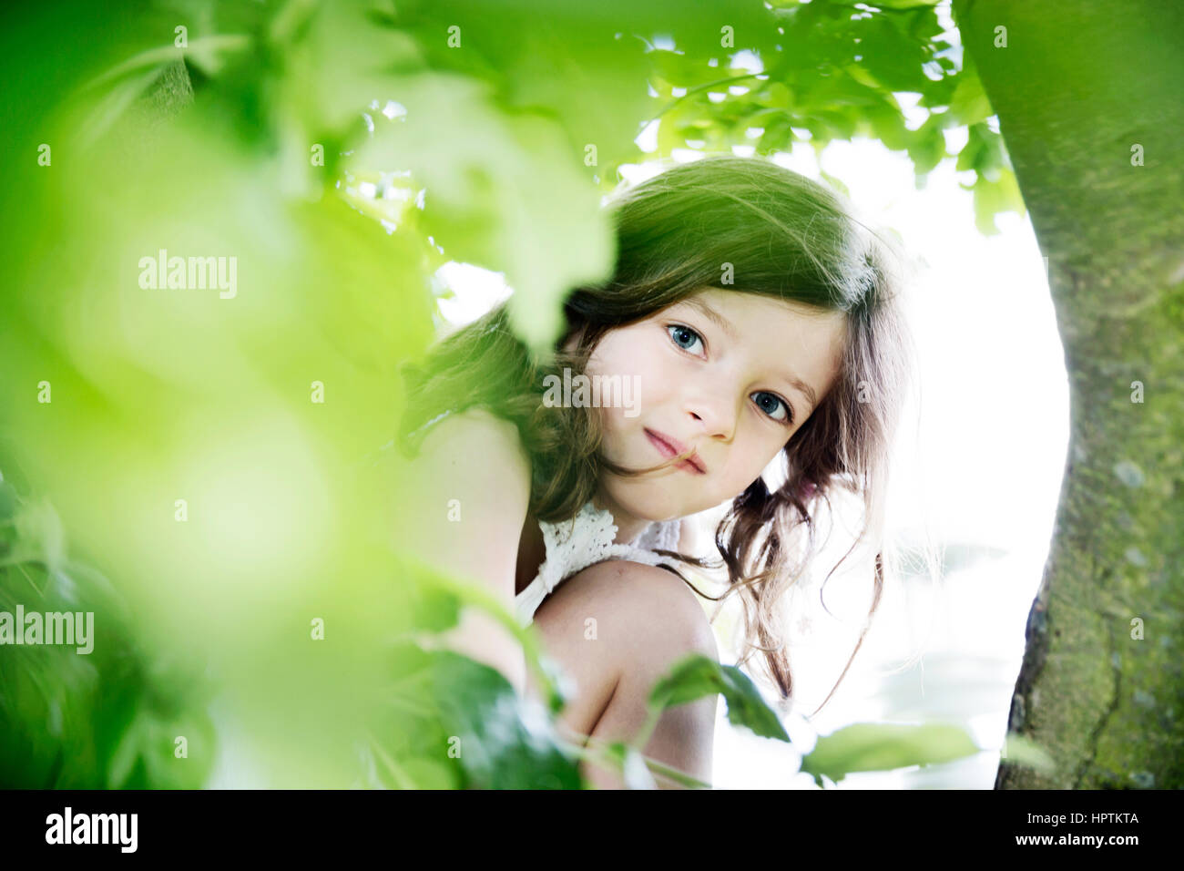 Girl crouching behind tree, looking at camera Stock Photo - Alamy