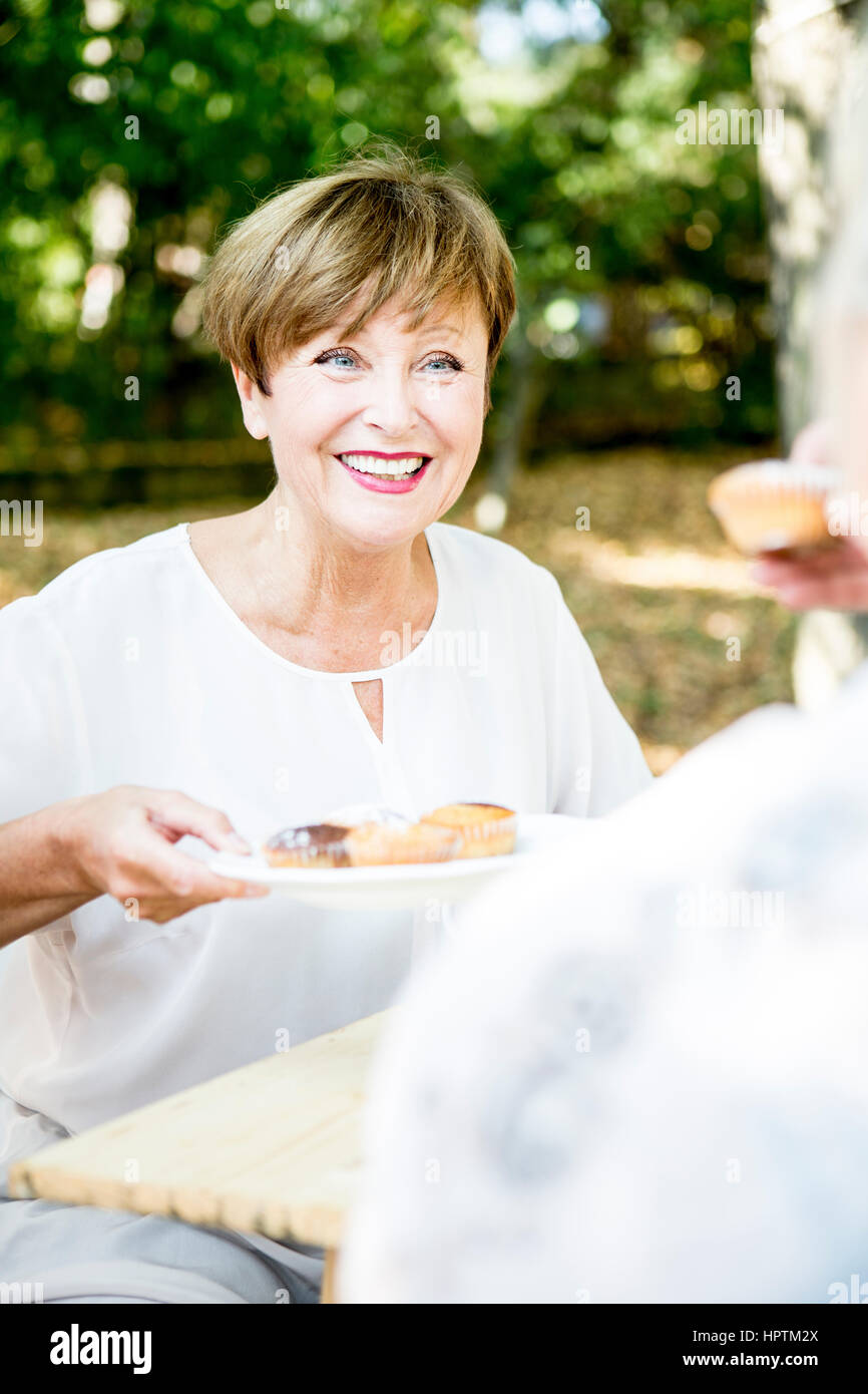 Smiling senior woman offering muffins Stock Photo - Alamy