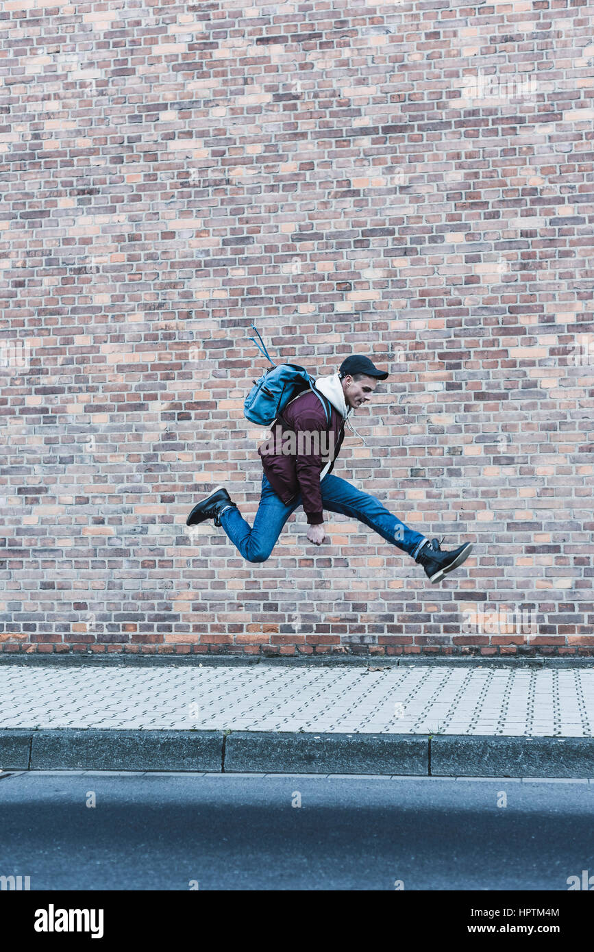 Young man jumping in front of brick wall Stock Photo - Alamy