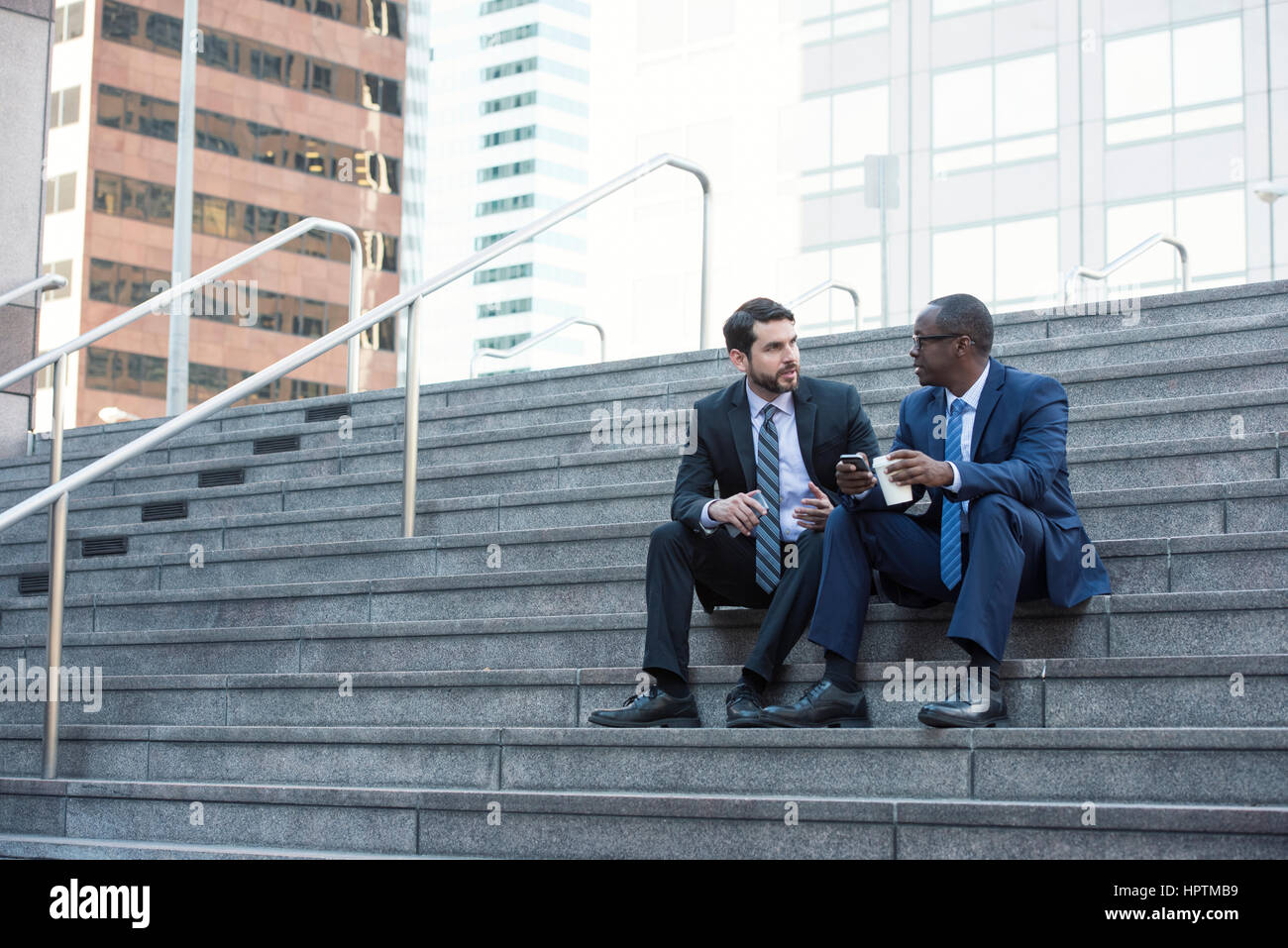 Two businessmen sitting on stairs talking Stock Photo - Alamy