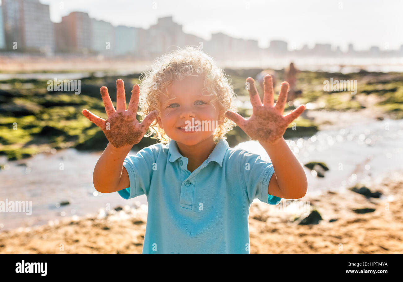 Portrait of smiling little boy showing his sandy hands on the beach ...