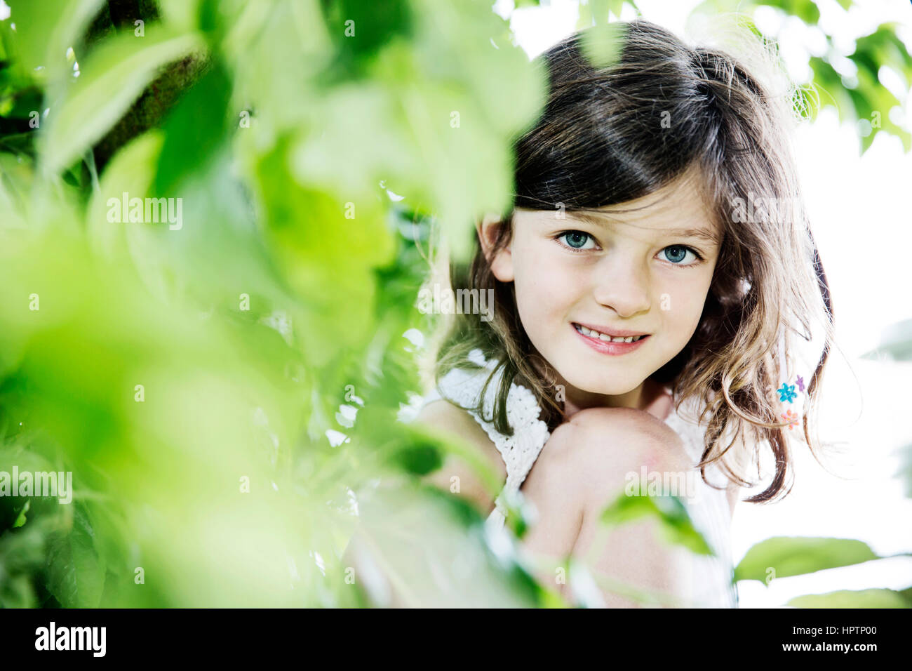 Girl crouching behind tree, looking at camera Stock Photo - Alamy