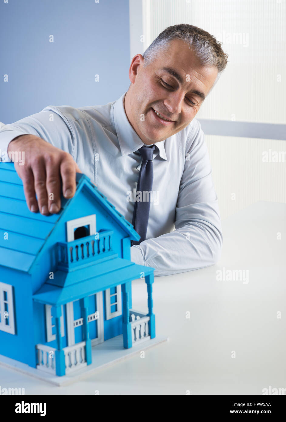 Real estate agent at desk with light blue model house Stock Photo - Alamy