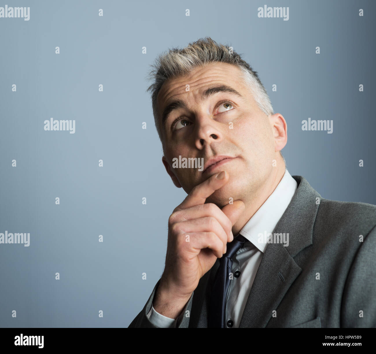 Handsome businessman with hand on chin looking up and thinking Stock ...