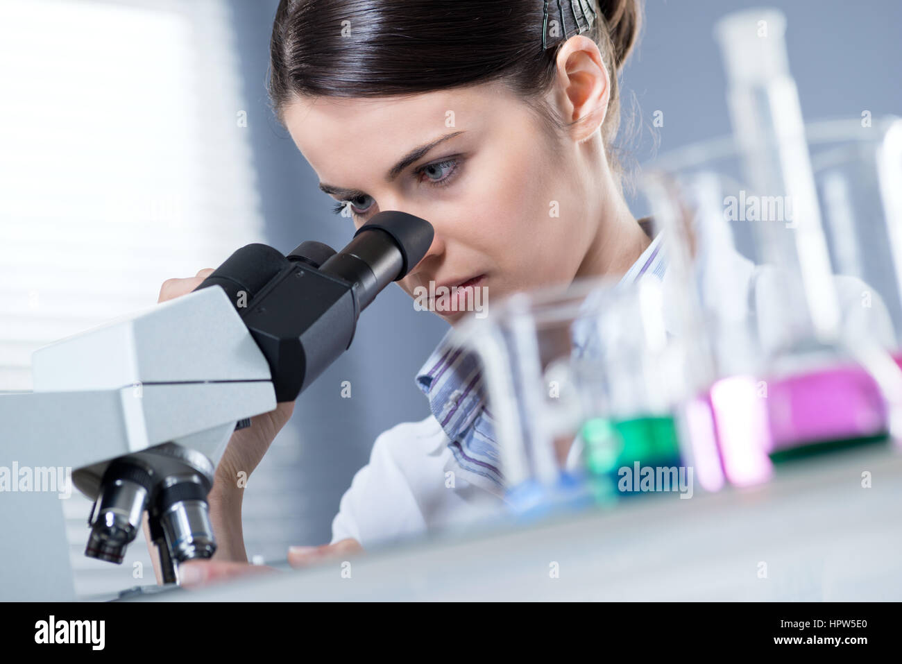 Young female researcher using microscope in the chemistry lab with ...