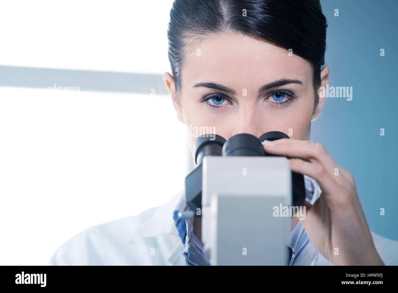 Attractive female researcher using microscope and looking at camera ...