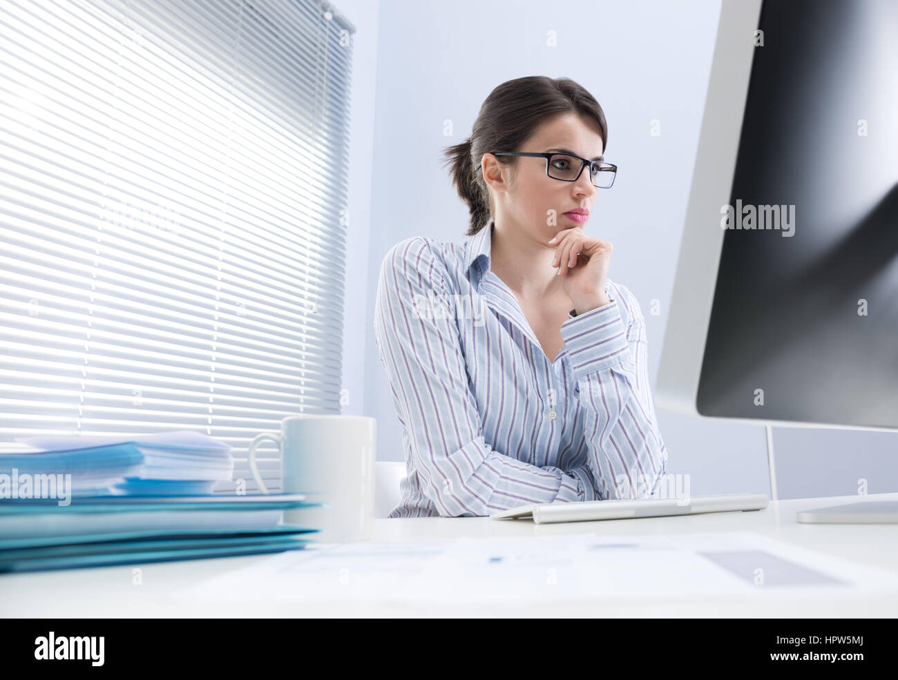 Pensive businesswoman staring at computer screen and touching her chin ...