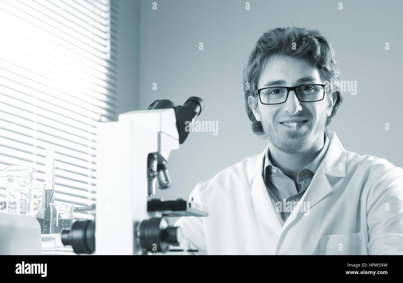 Student researcher using microscope and smiling at camera Stock Photo ...