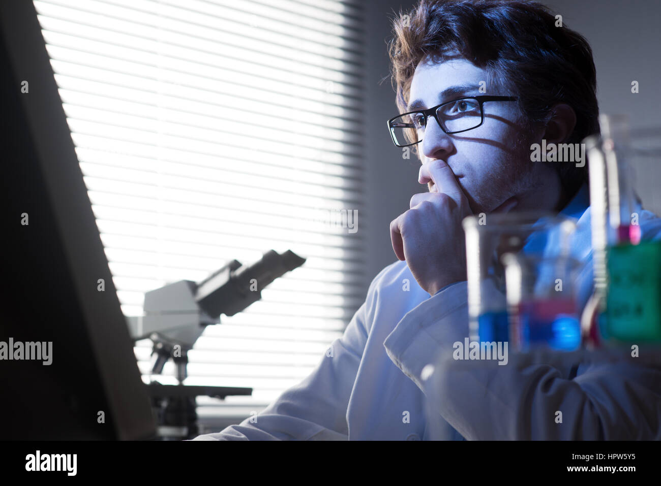 Researcher working at computer in the laboratory with hand on chin ...