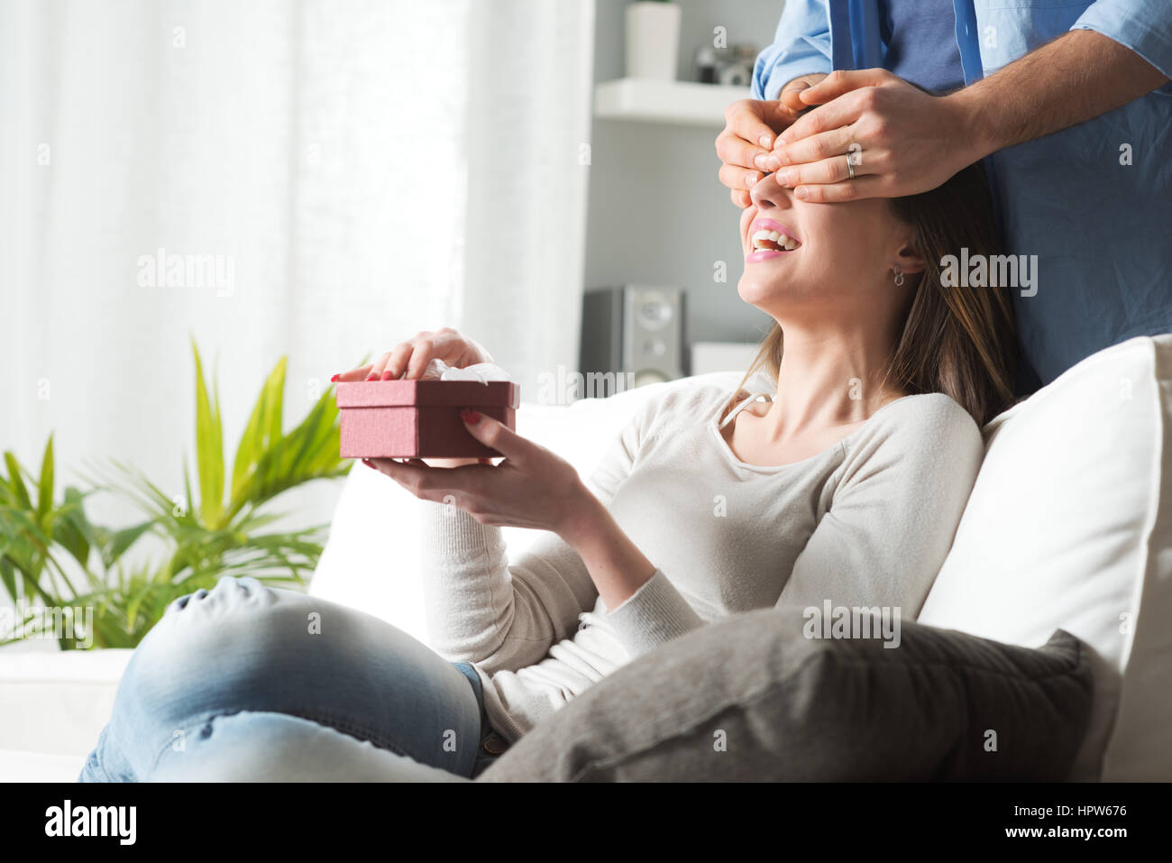 Young woman receiving a surprise gift box from her boyfriend at home ...