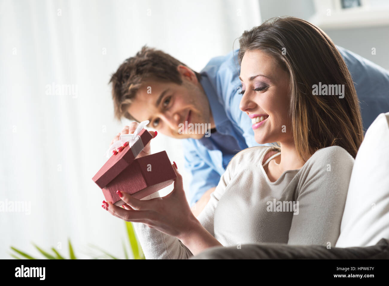 Young woman receiving a surprise gift box from her boyfriend at home ...