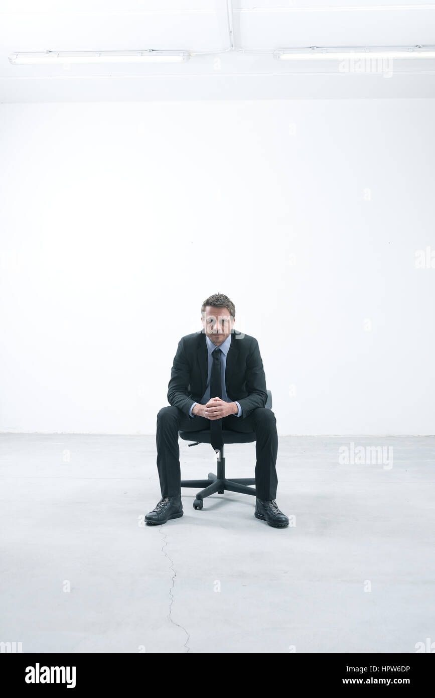 Elegant businessman sitting on an office chair in an empty room looking ...