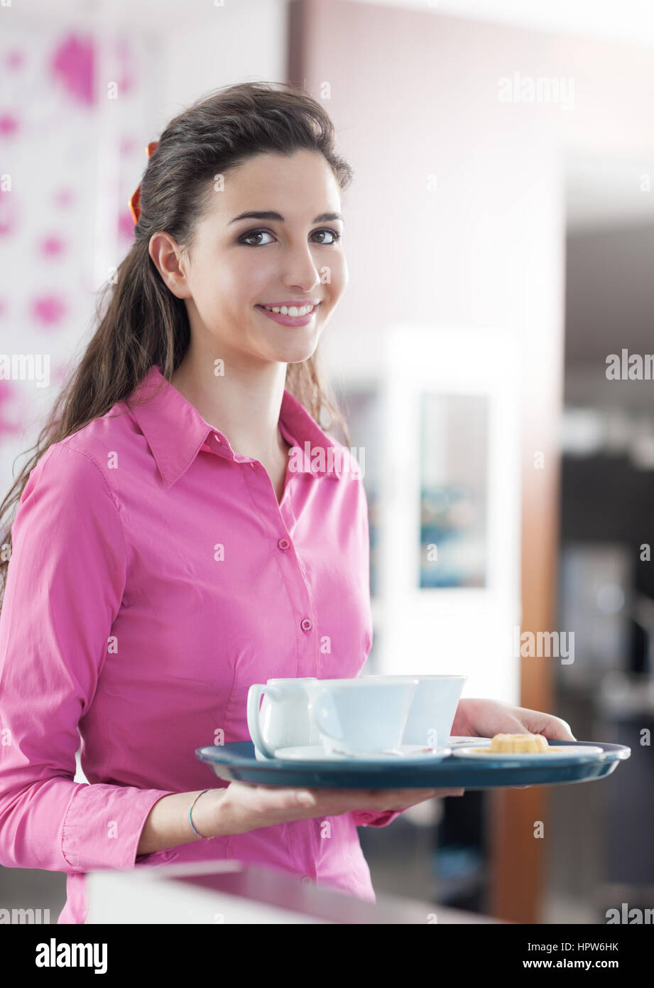 Young smiling waitress in pink shirt serving coffee at the bar, floral ...