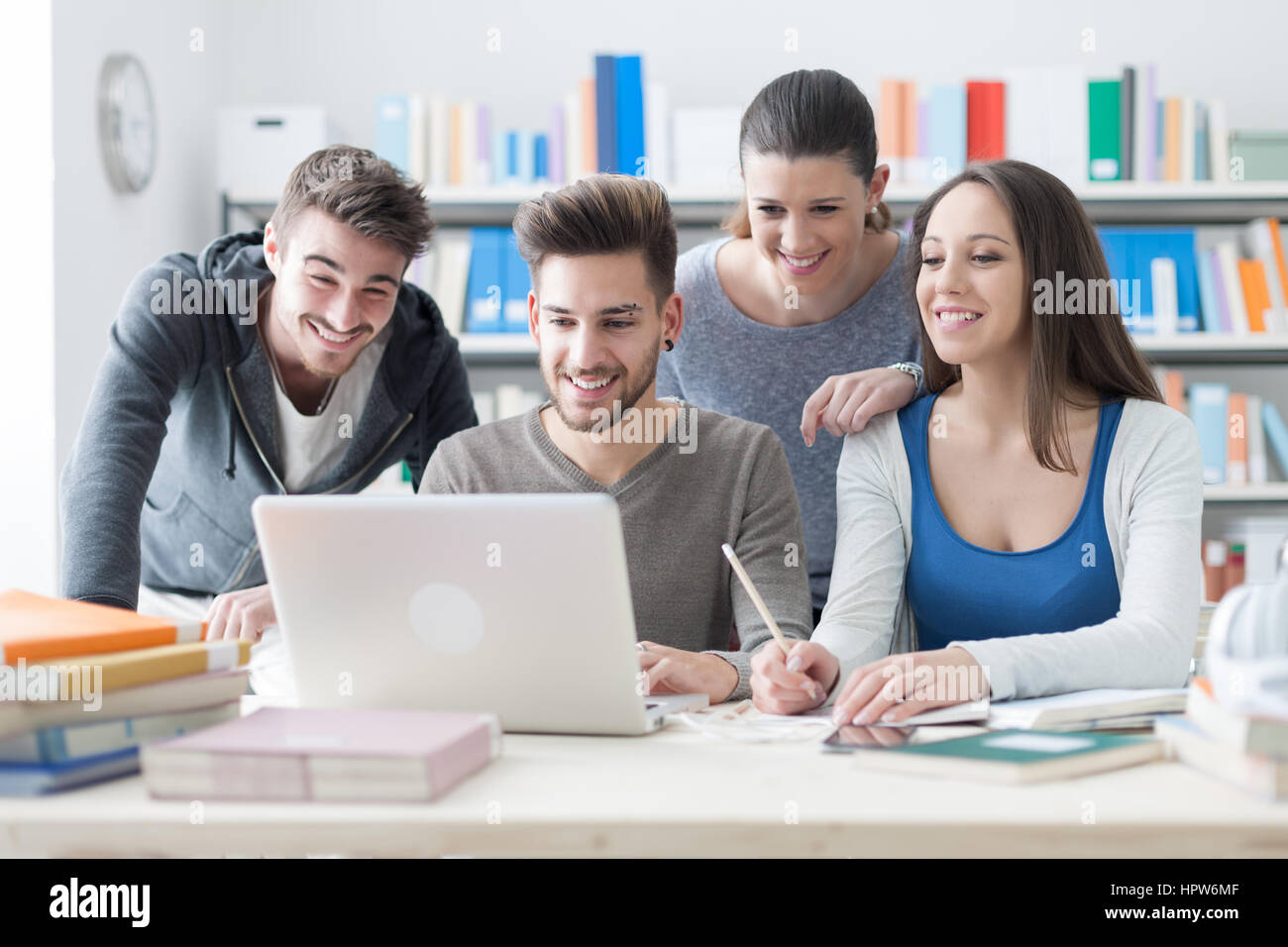 Group of smiling college students using a laptop and studying together ...