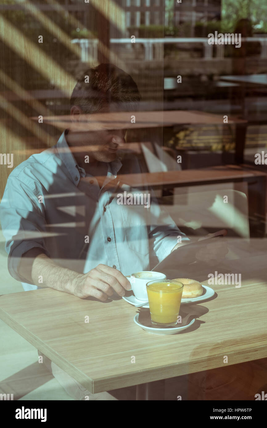 Man having breakfast at the cafe next to a window with reflections ...