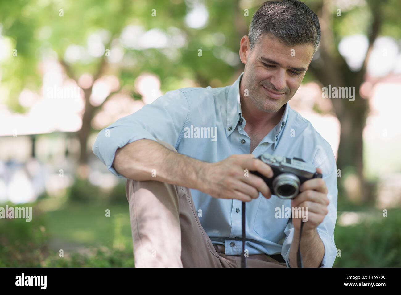 Smiling photographer at the park, he is sitting and watching picture ...