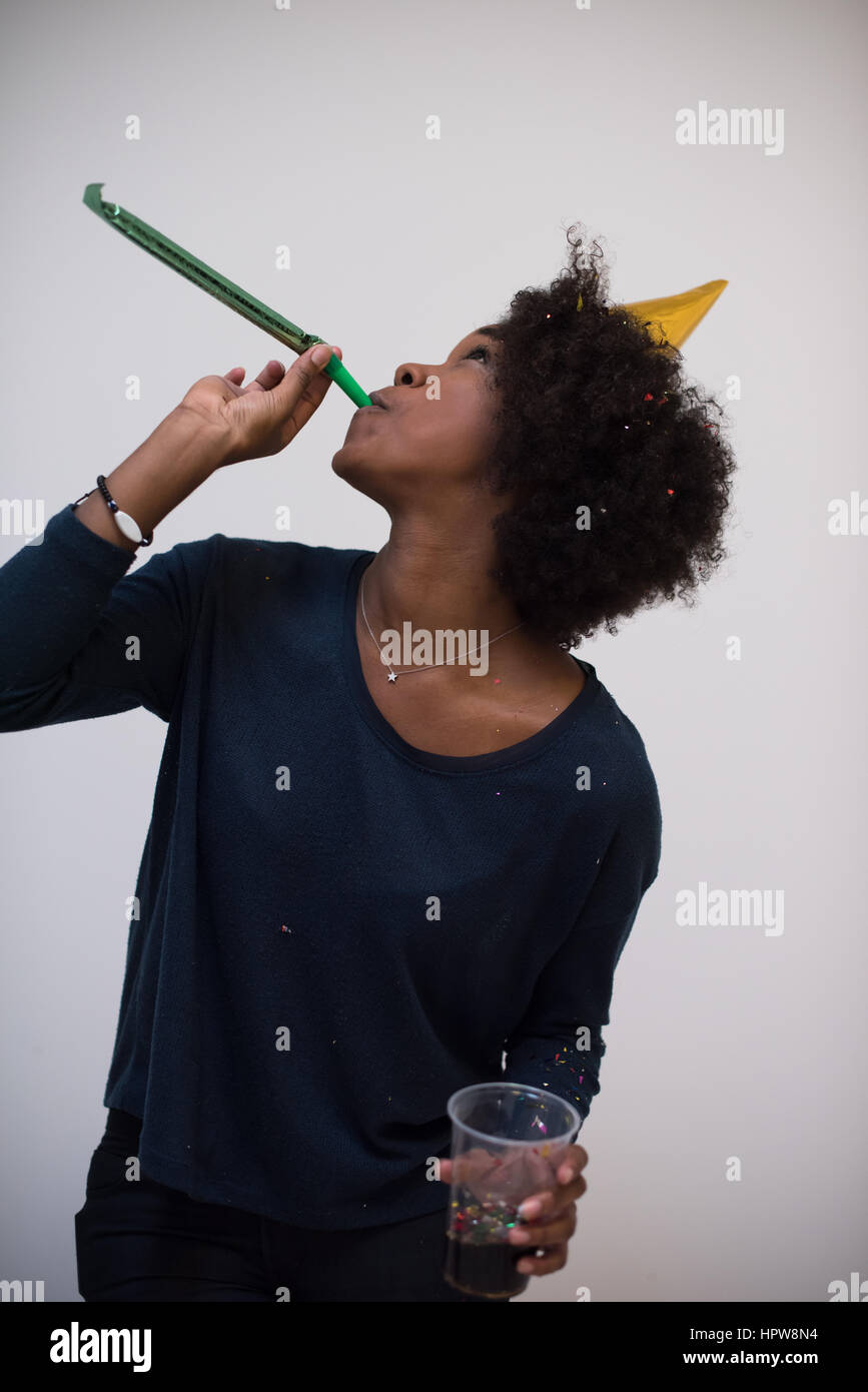 portrait of a young beautiful black woman in party hat blowing in ...