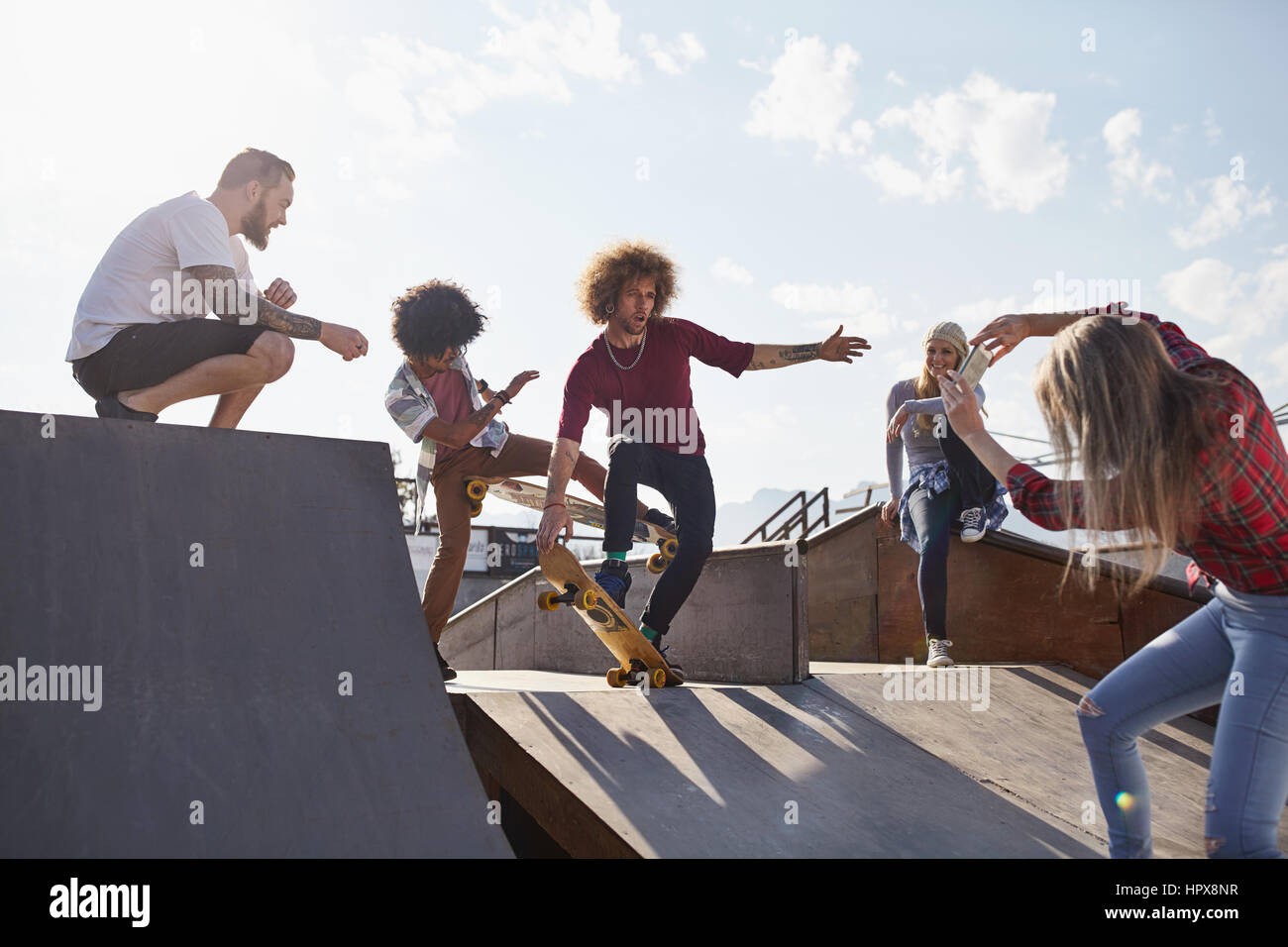 Woman photographing male friends skateboarding on ramp at sunny skate ...