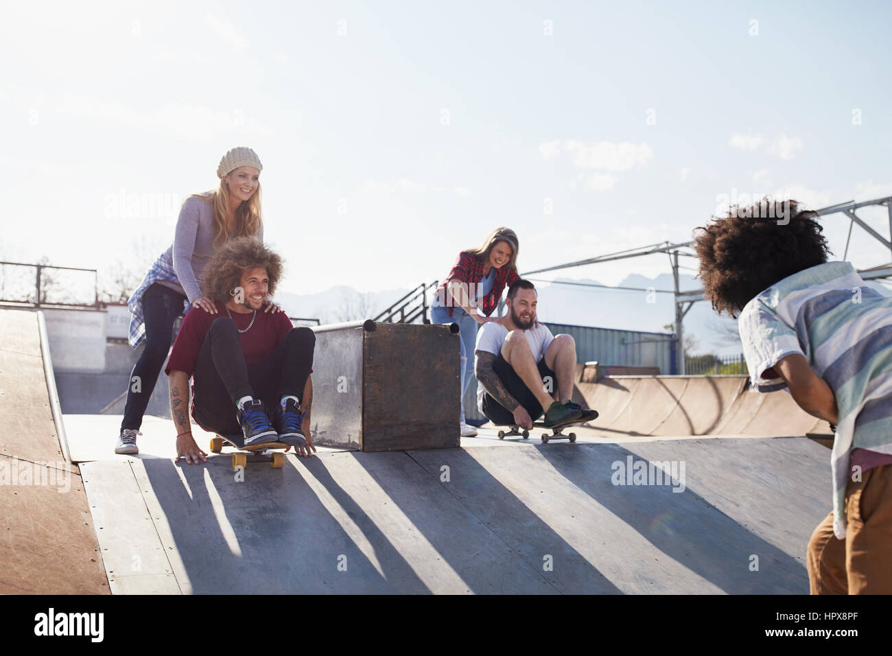 Friends pushing each other on skateboards at sunny skate park Stock ...