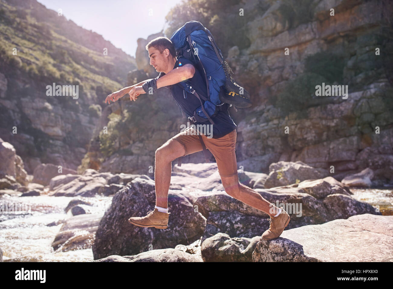 Young man with backpack hiking, jumping rocks Stock Photo - Alamy