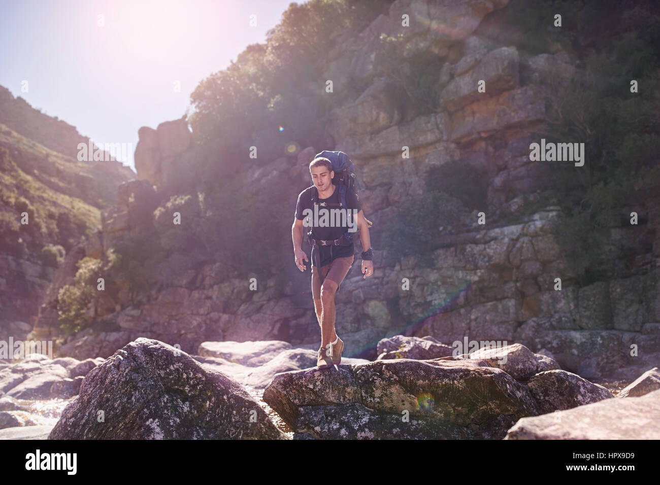 Young man with backpack hiking over sunny rocks Stock Photo - Alamy