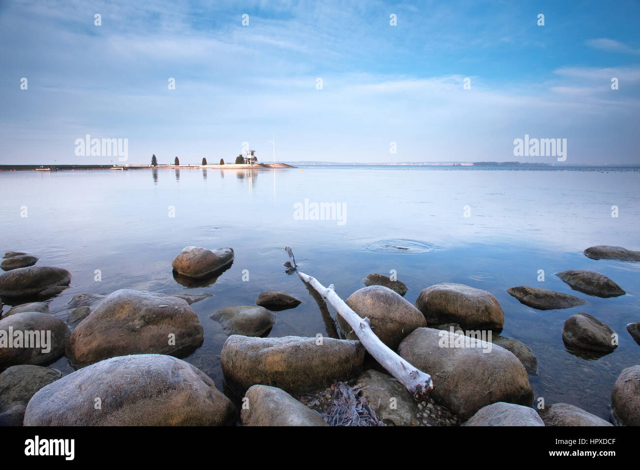 coast of still lake with stones on front Stock Photo - Alamy