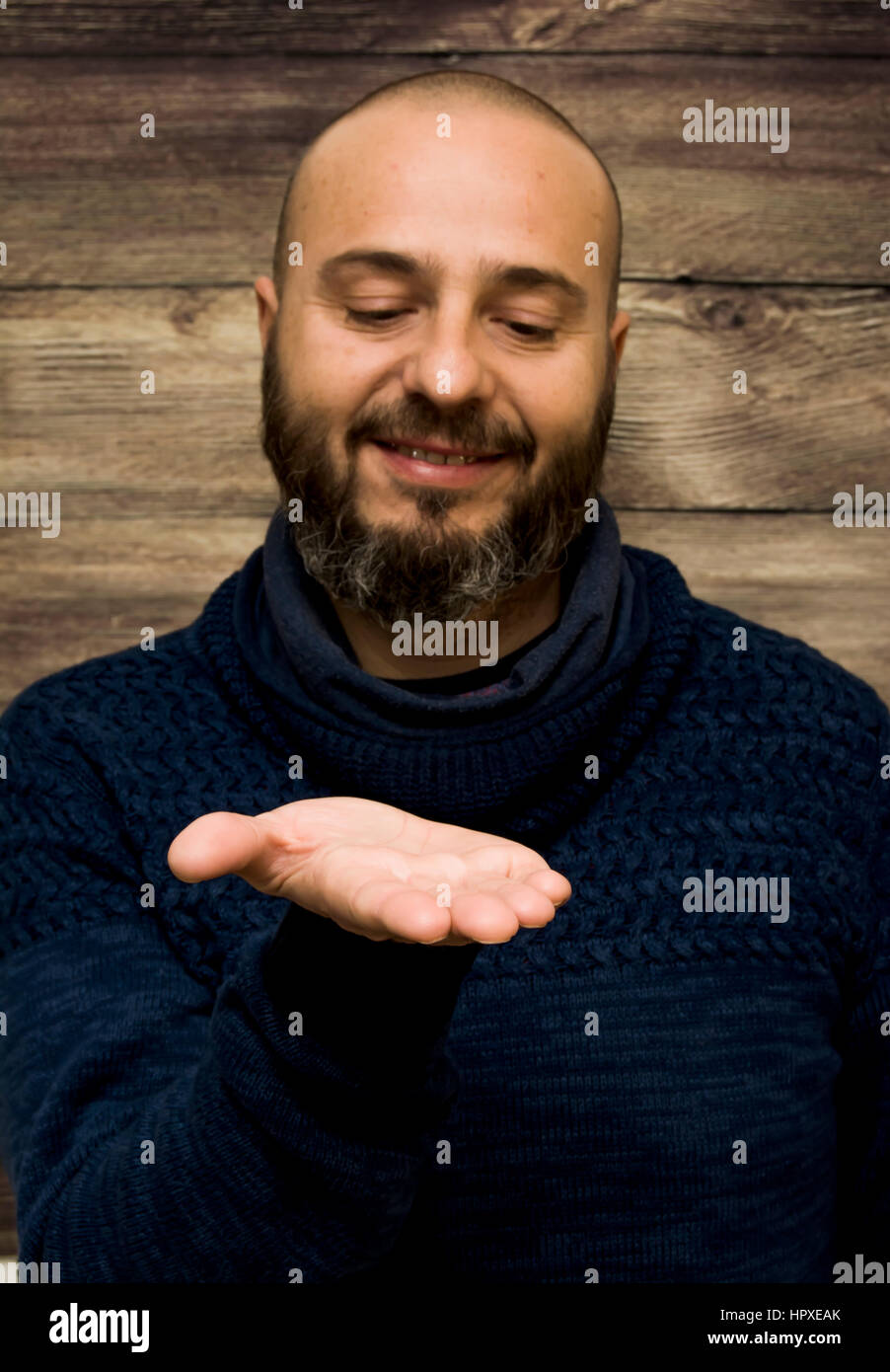Handsome, bald man with beard with his open hand on a wooden background ...