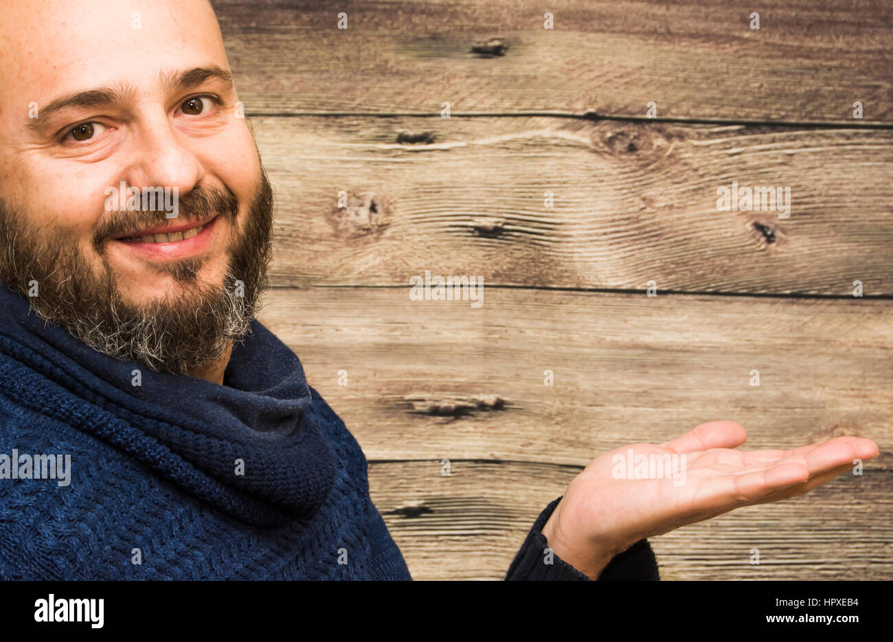Handsome, bald man with beard with his open hand on a wooden background ...