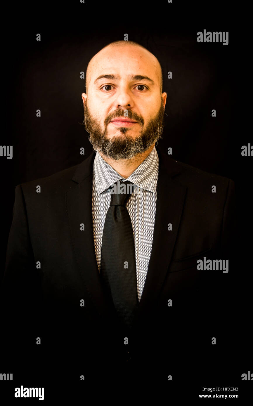 Handsome, bald man with beard, in suit and tie, on black background ...