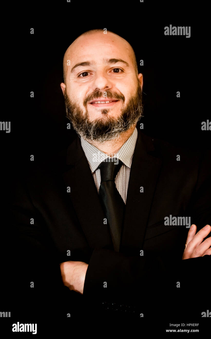 Handsome, bald man with beard, in suit and tie, on black background ...