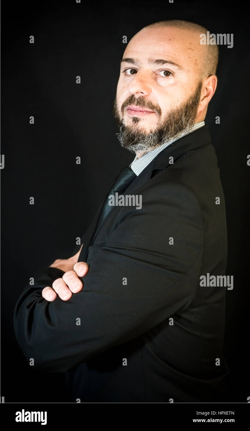 Handsome, bald man with beard, in suit and tie, on black background ...