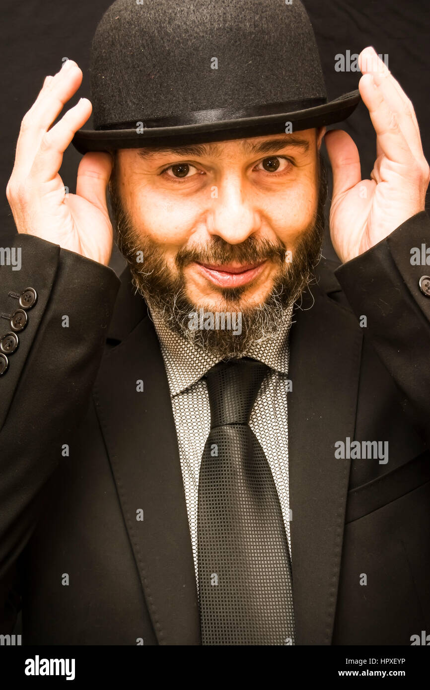 Handsome, bald man with beard, suit, tie and hat, on black background ...